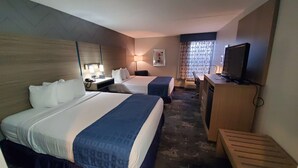 Quarto de hotel com duas camas, uma escrivaninha, uma televisão e uma janela com cortinas estampadas.