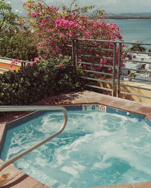 Hidromassagem com vista para o mar, rodeada por flores cor-de-rosa e um guarda-corpo de metal.