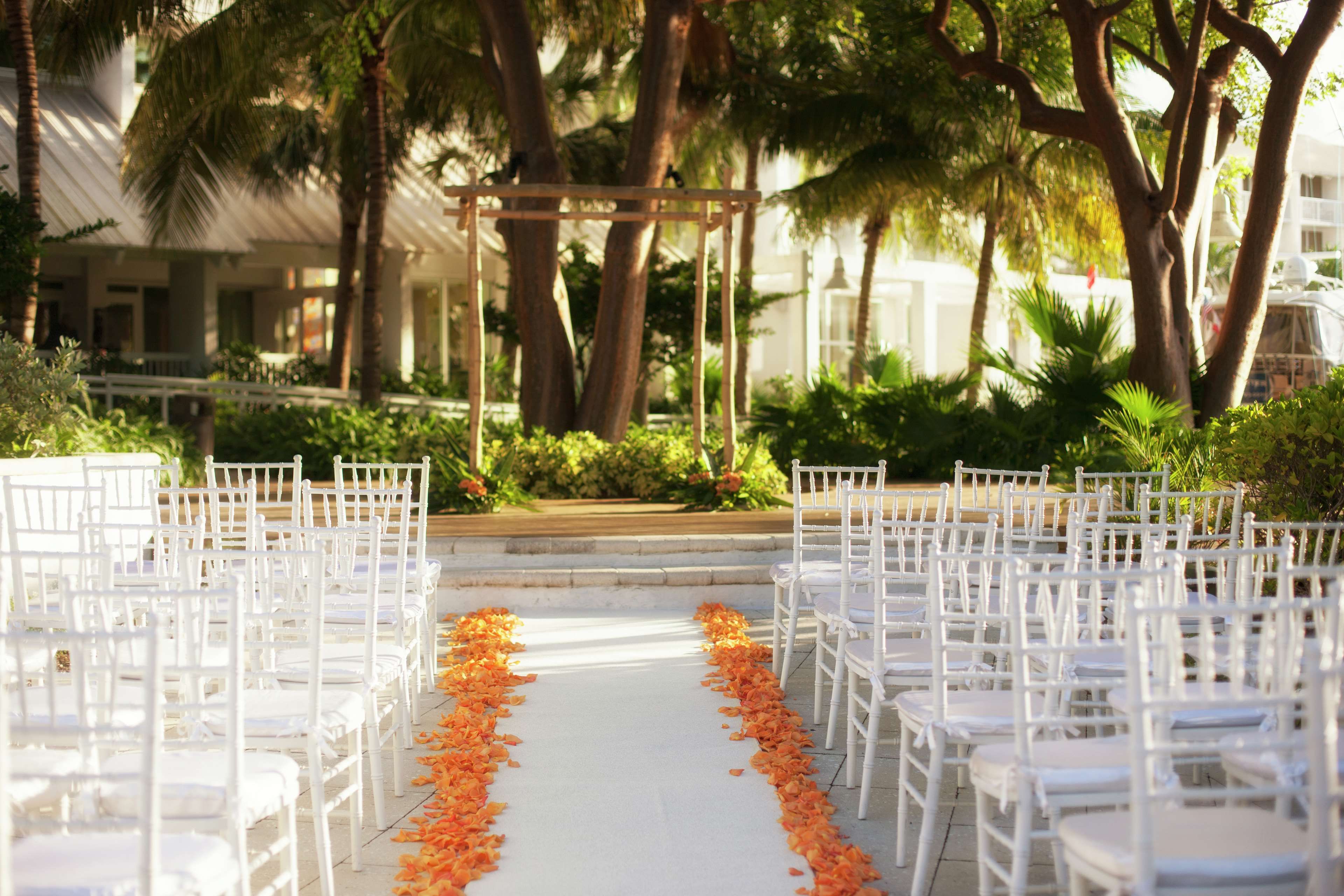 Um corredor de casamento com cadeiras brancas e um caminho de flores.