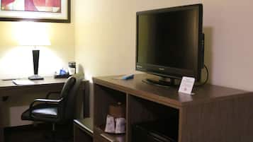Quarto de hotel com escrivaninha, computador, cadeira, refrigerador e um quadro na parede.
