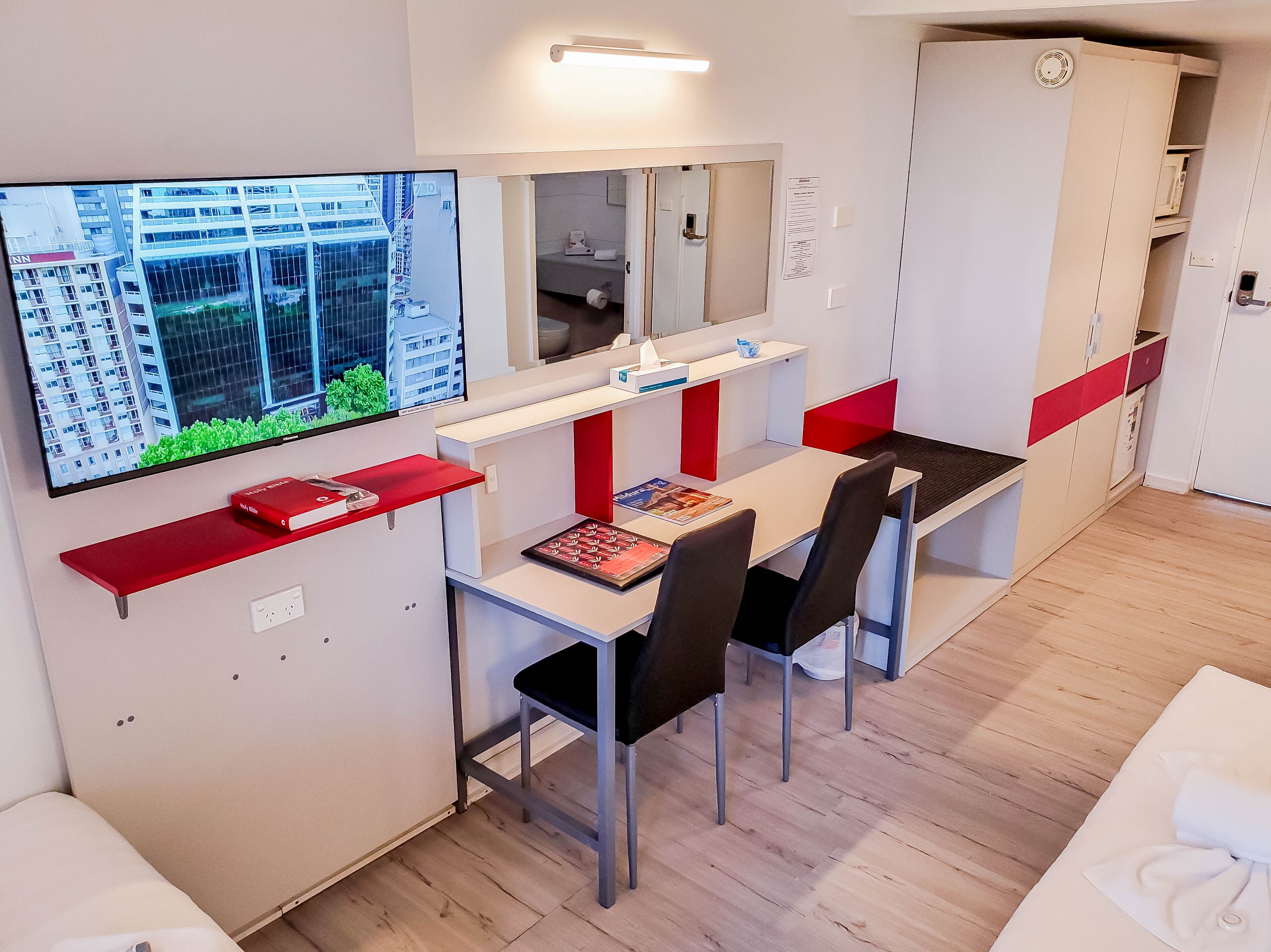 Quarto de hotel moderno com área de jantar, televisão na parede e espelho sobre o balcão.
