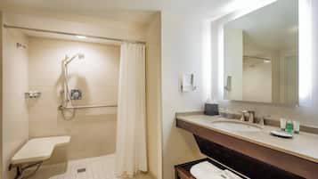 Uma casa de banho moderna com chuveiro, sanita, lavatório e um espelho grande.