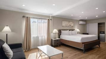 Quarto de hotel com cama, mesas de cabeceira, escrivaninha, sofá e janela com cortinas.