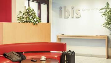 Uma área de estar vermelha com uma mesa, uma mala preta e uma placa com a inscrição 'ibis'.