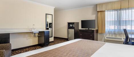 Quarto de hotel com uma cama grande, uma escrivaninha com cadeira, televisão, minibar e janela com cortinas.