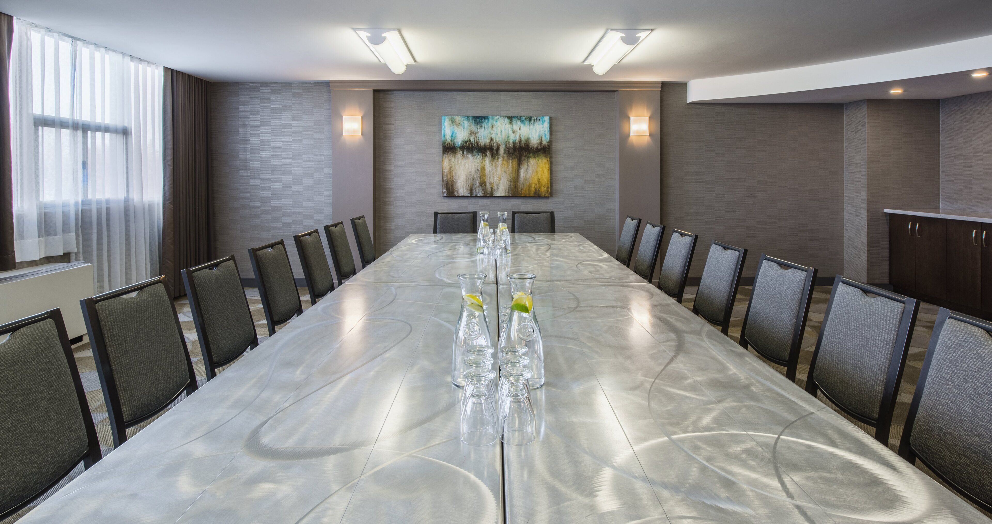 Uma sala de conferência com uma mesa comprida, cadeiras e um quadro na parede.
