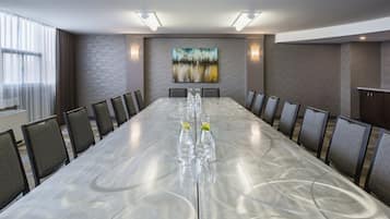 Uma sala de conferência com uma mesa comprida, cadeiras e um quadro na parede.