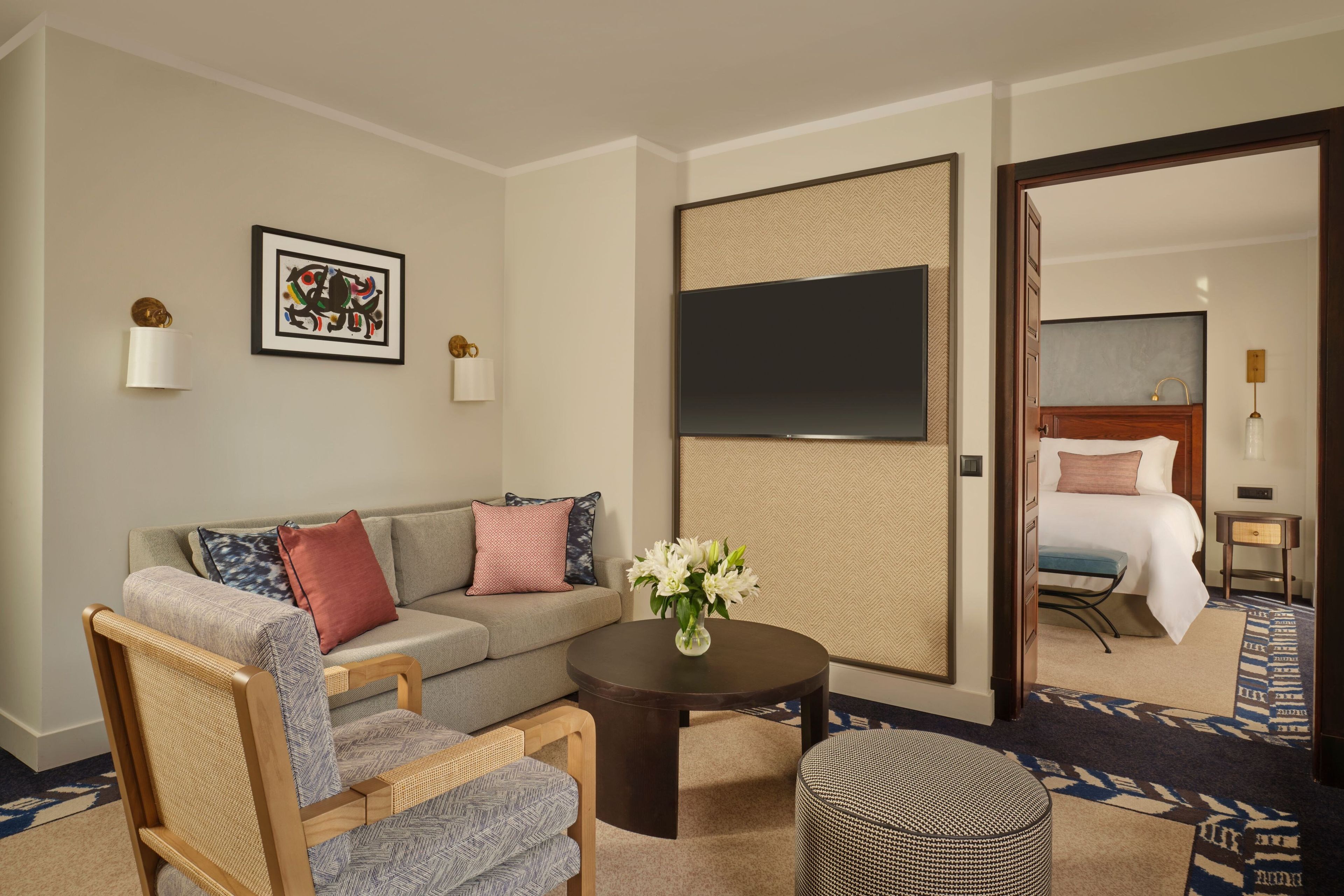 Quarto de hotel com sofá, poltrona, mesa de centro e televisão na parede.