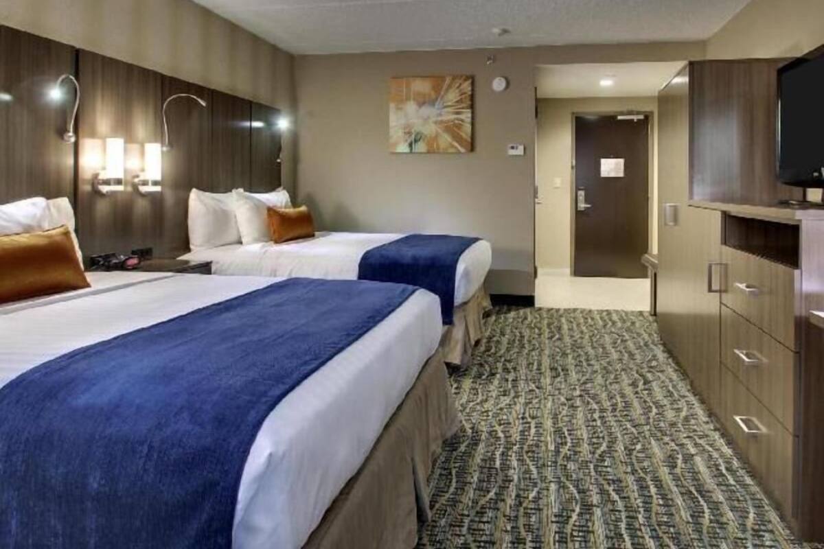 Quarto de hotel com duas camas, televisão, quadro na parede e piso coberto por carpete.