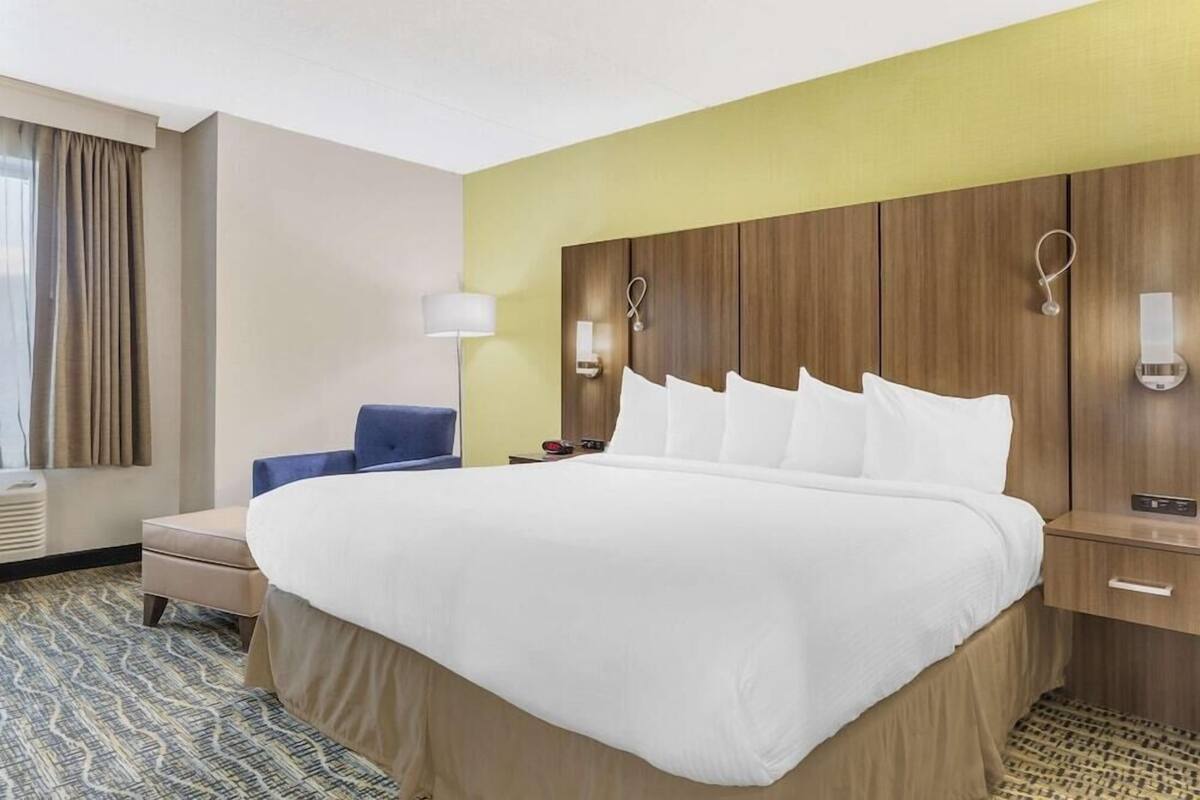 Quarto de hotel com cama grande, escrivaninha, cadeira, abajur e luminária na parede.