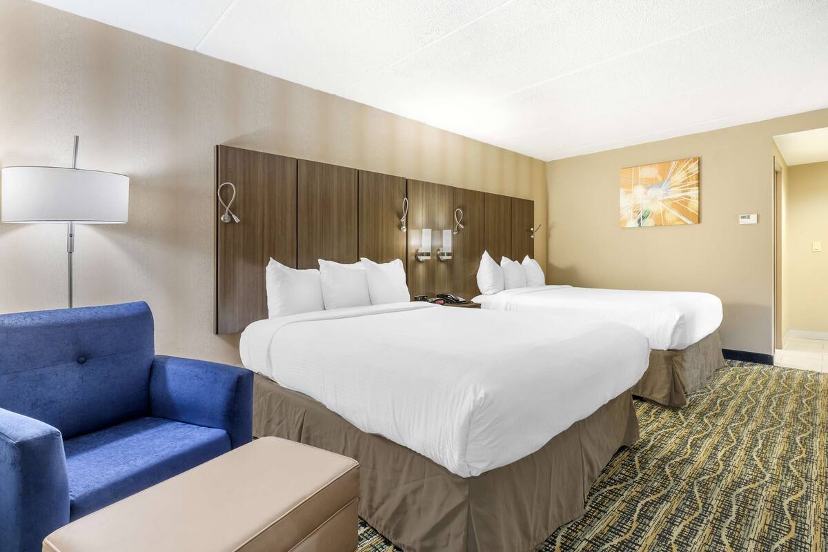 Quarto de hotel com duas camas, um sofá, uma escrivaninha e uma luminária.