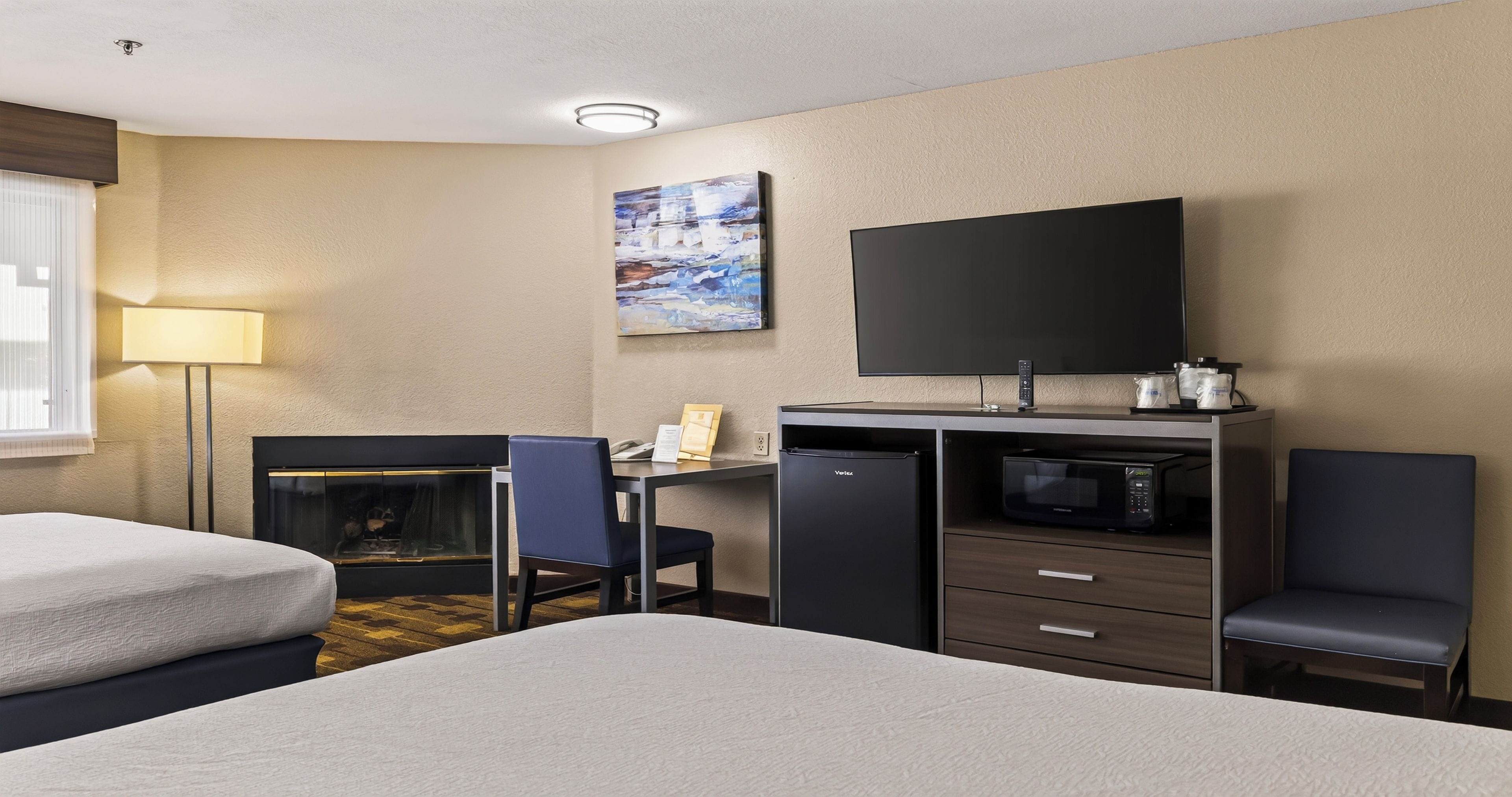 Quarto de hotel com cama, escrivaninha, cadeira, televisão e micro-ondas.
