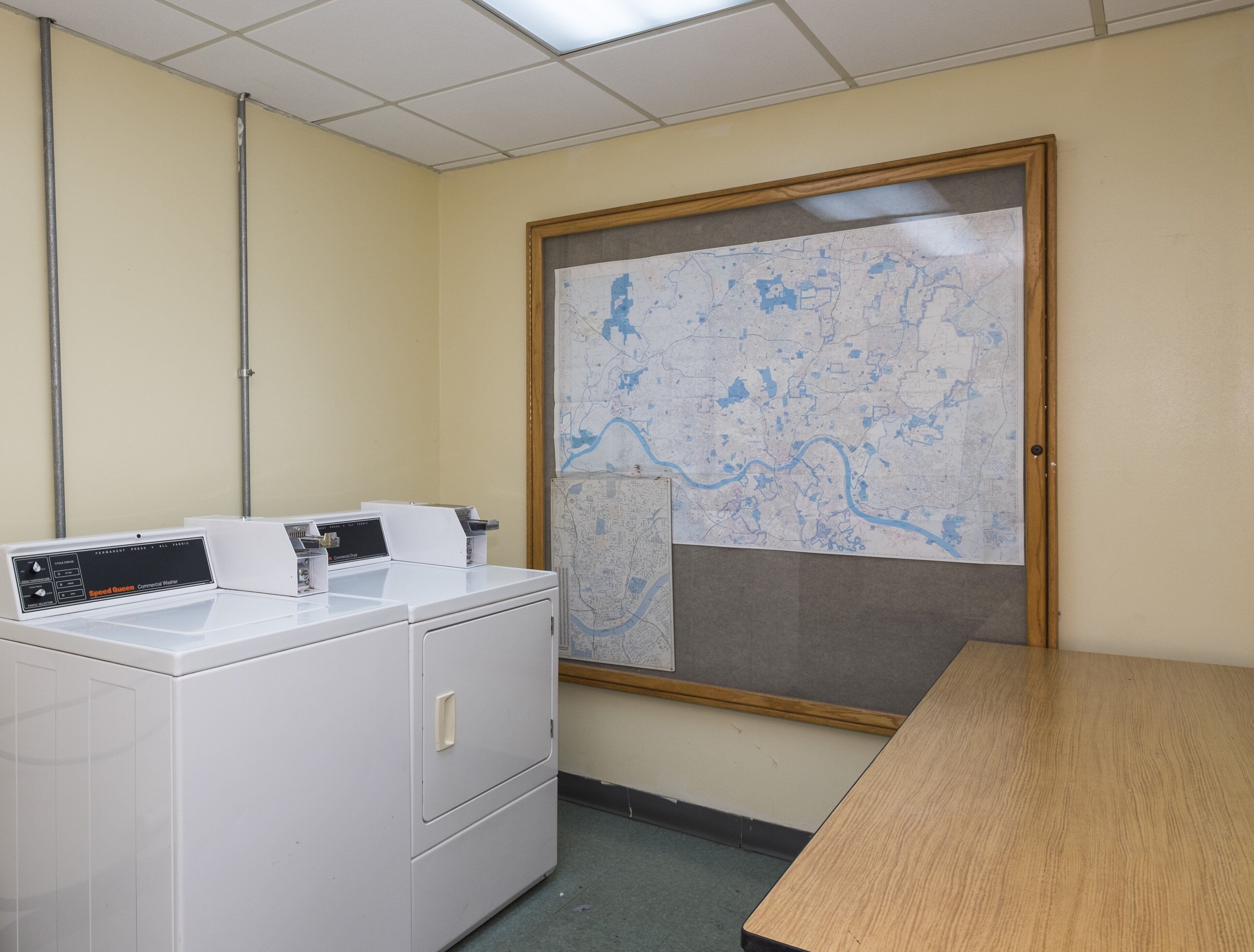 Quarto com mapa na parede, máquina de lavar industrial e mesa de madeira.
