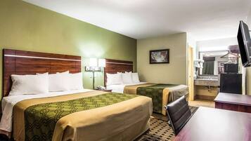 Quarto de hotel com duas camas, uma secretária, uma cadeira, televisão e casa de banho visível por uma porta aberta.