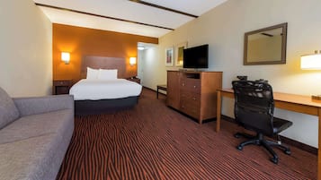 Quarto de hotel com cama, escrivaninha, cadeira, televisão e espelho.