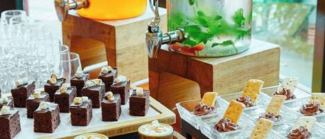 Um buffet com diversas opções de comida e bebida, incluindo um jarro grande de chá gelado, um aquário e várias bandejas de sobremesas e petiscos.