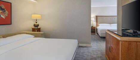 Quarto de hotel com uma cama grande, uma televisão, mesa de cabeceira com abajur e uma mesinha com um objeto decorativo.
