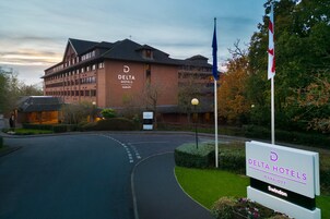 Edifício do Delta Hotels Marriott com design arquitetônico moderno, um gramado bem cuidado e uma estrada clara que leva à entrada.