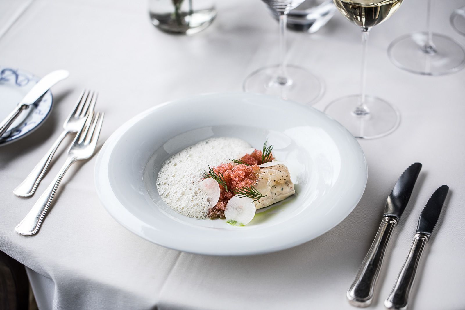 Um prato branco com um prato de peixe, acompanhado de um garfo e uma faca sobre a mesa.
