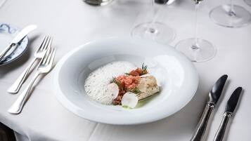 Um prato branco com um prato de peixe, acompanhado de um garfo e uma faca sobre a mesa.
