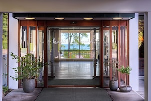 Entrada de hotel com porta de vidro, moldura de madeira e vista para uma paisagem verde.