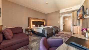Quarto de hotel com cama, sofá, escrivaninha e televisão.