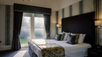 Quarto com cama grande, cabeceira, mesa de cabeceira, abajur e janela com cortinas.