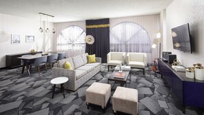 Quarto de hotel moderno com área de refeições, sofá, mesa de centro e televisão.
