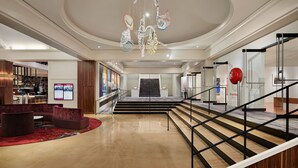 Um hall amplo com escadaria moderna, tapete vermelho e um lustre.