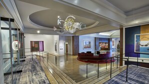 Um hall amplo com um lustre moderno, uma área de estar vermelha e um guarda-corpo de vidro.