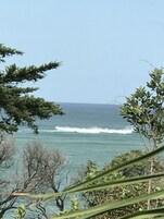 Vista costeira com ondas quebrando na praia, rodeada por árvores e vegetação.