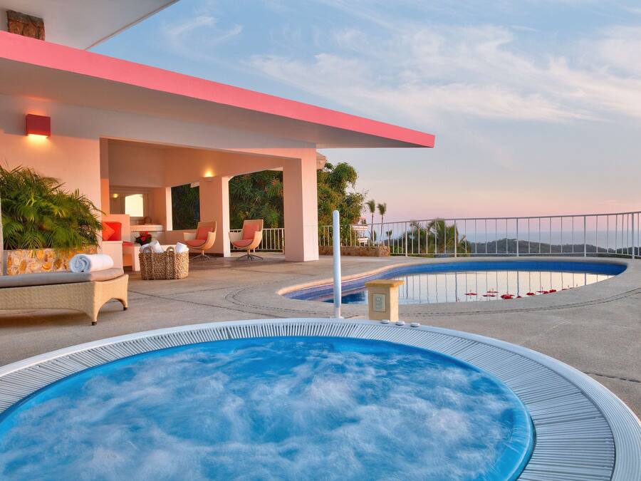 Uma área de piscina no terraço com espreguiçadeiras, uma banheira de hidromassagem e vista para o mar.