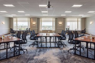 Sala de conferências com uma mesa grande, várias cadeiras, um projetor e janelas amplas com vista para a cidade.