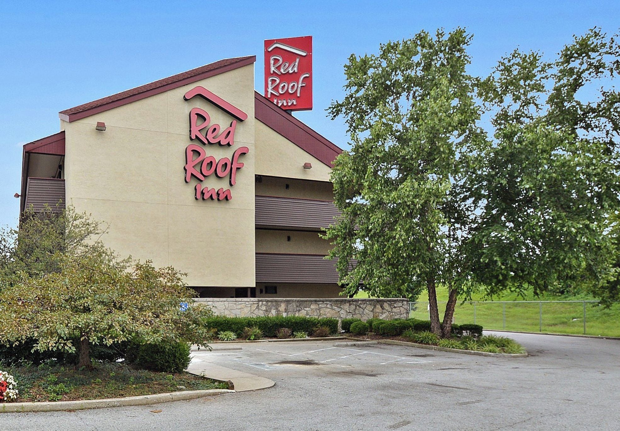 Um Red Roof Inn com fachada bege, telhado vermelho e estacionamento.