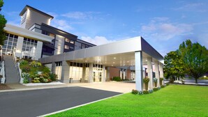 Entrada moderna de hotel com galeria coberta, jardim ajardinado e céu limpo.