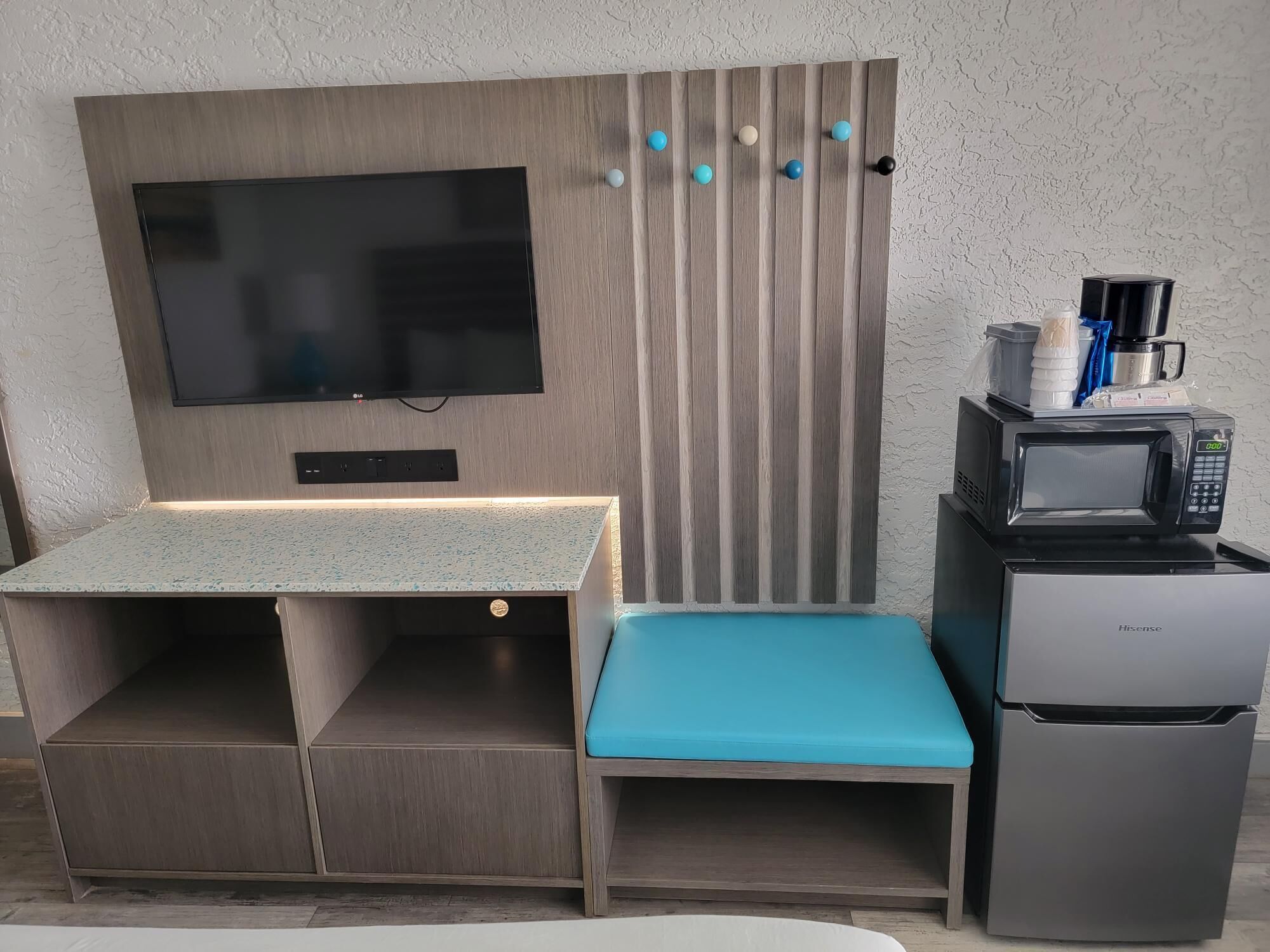 Uma cozinha compacta equipada com televisão de tela plana, micro-ondas, geladeira e um pequeno espaço de estar com um banco.