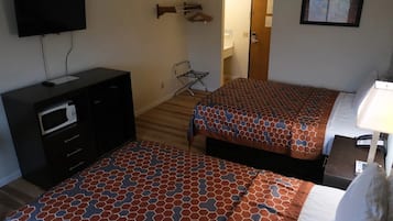 Quarto de hotel com duas camas, televisão, micro-ondas, escrivaninha com luminária e porta de acesso a um banheiro.