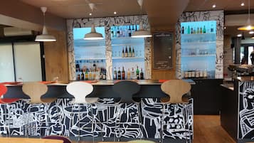 Uma área de bar com balcão, prateleiras com garrafas e uma parede com um mural.