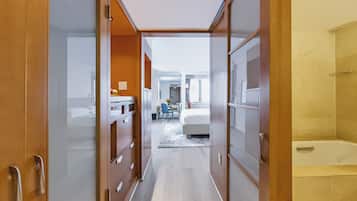 Corredor que leva a um quarto com uma cama, uma escrivaninha e uma cadeira. Banheiro com banheira visível à direita.