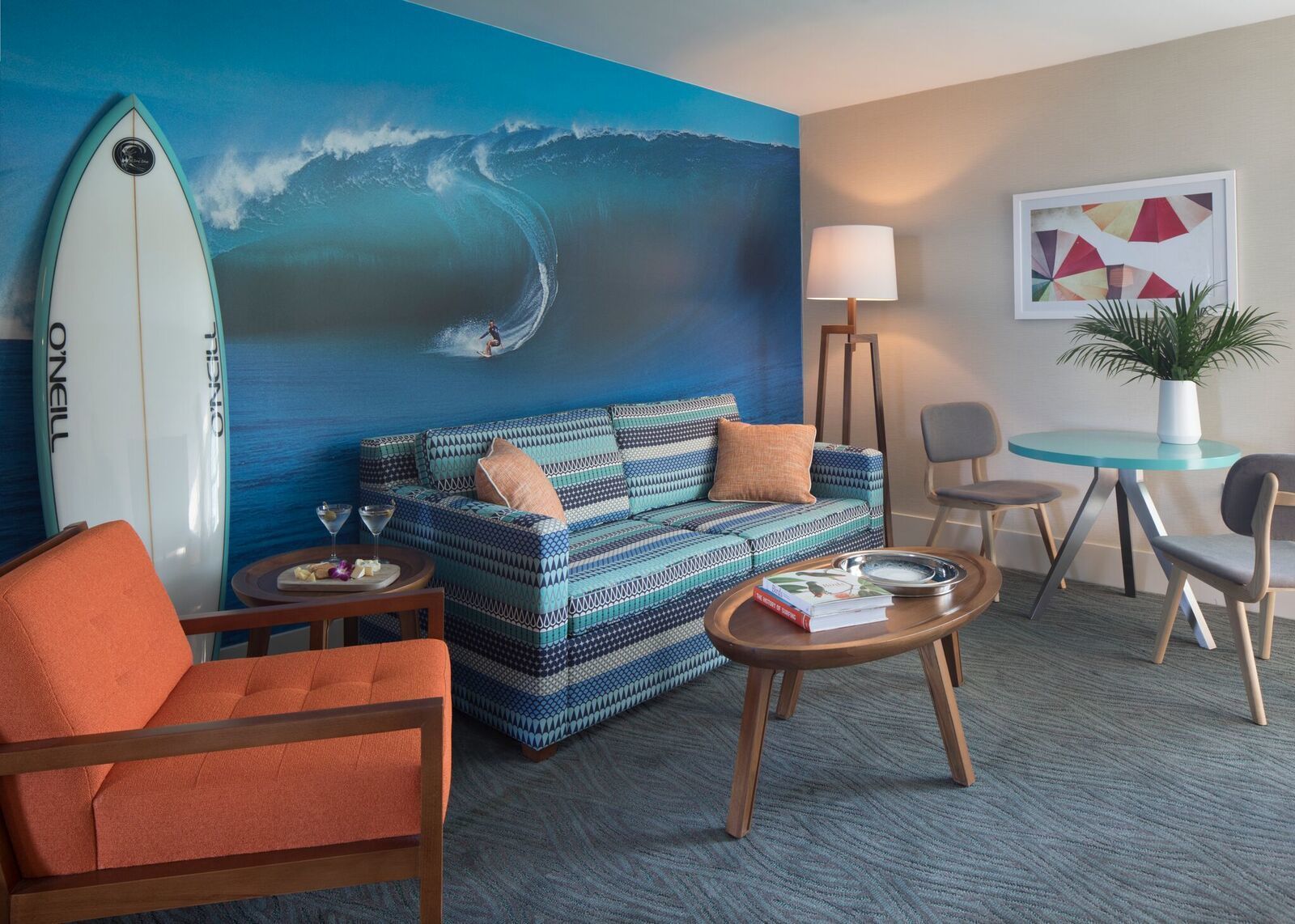 Quarto com um grande mural de uma onda do mar, um sofá, uma mesa de centro, uma cadeira e um prancha de surf.