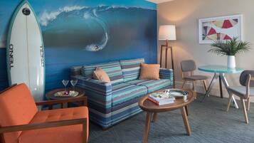 Quarto com um grande mural de uma onda do mar, um sofá, uma mesa de centro, uma cadeira e um prancha de surf.