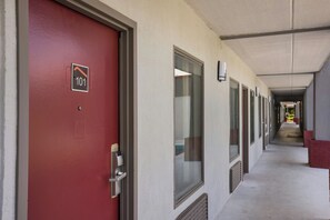 Corredor com uma porta vermelha identificada com o número '101' e uma série de janelas ao longo da parede.
