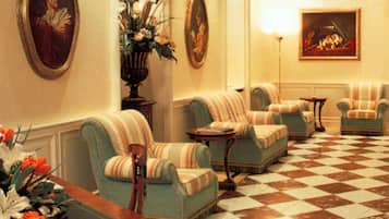 Um quarto com piso xadrez, uma mesa de madeira com um vaso de flores e três poltronas listradas.