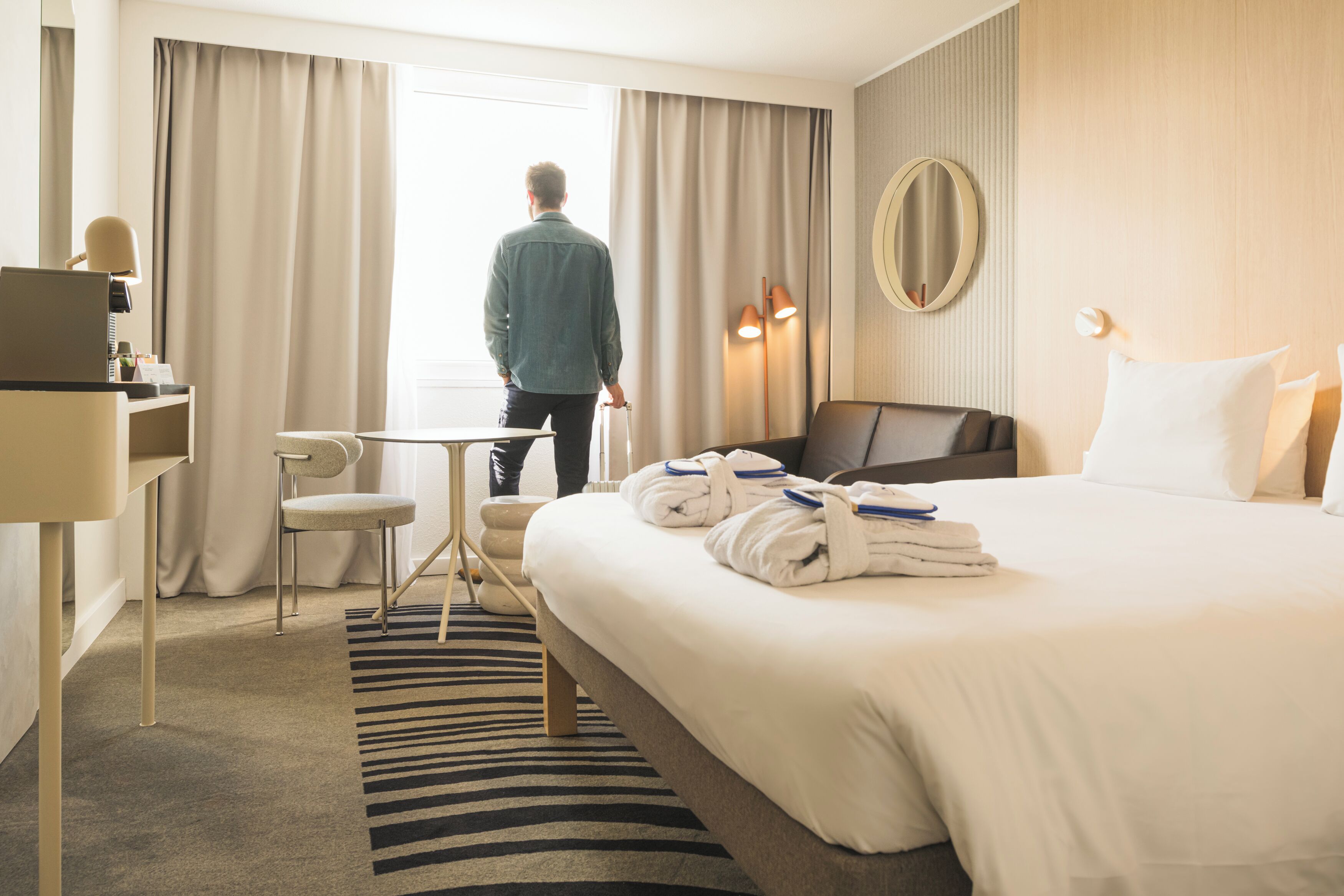 Quarto de hotel com uma cama, uma mesa, uma cadeira, um laptop e vista para o exterior.