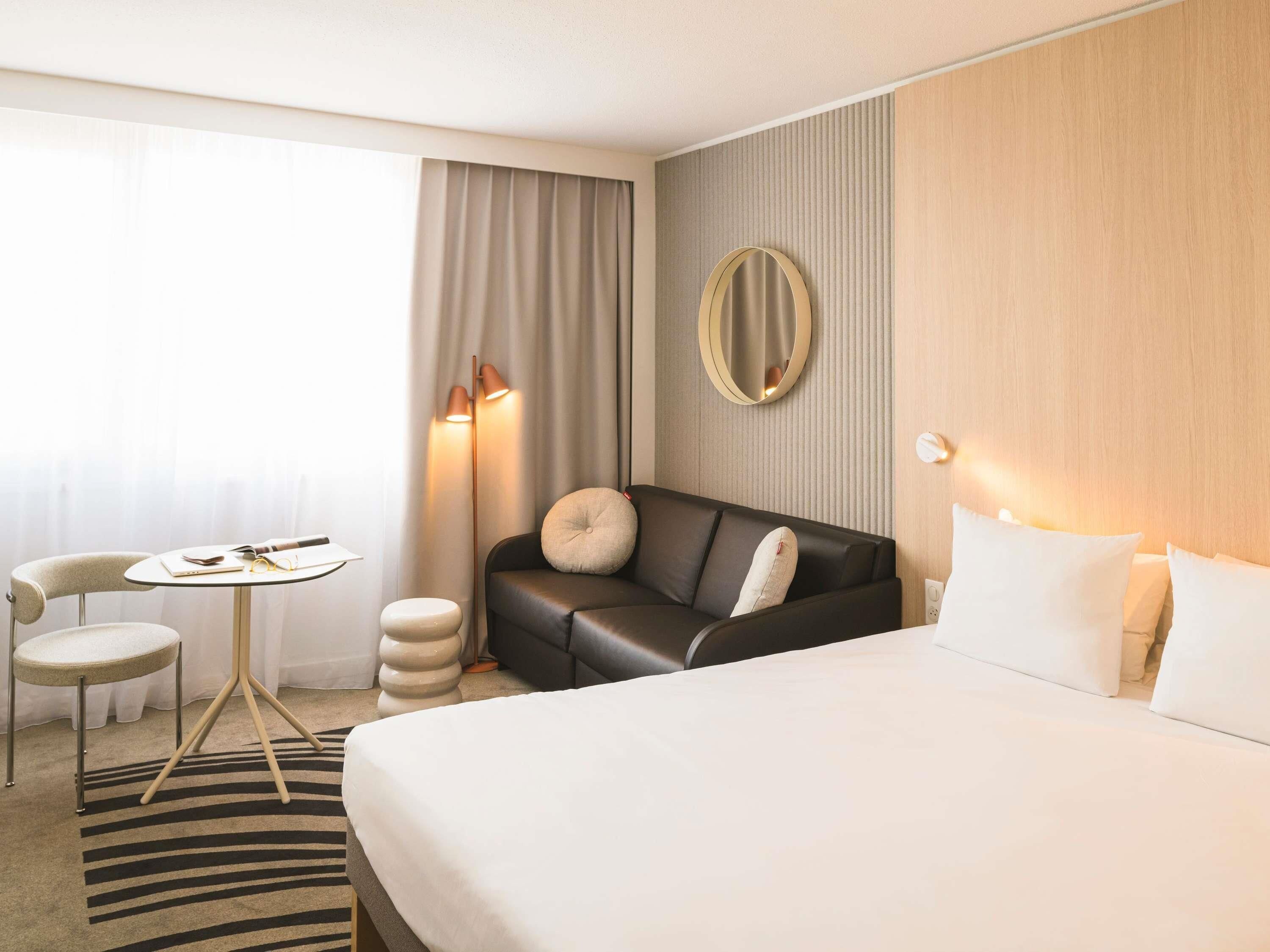 Quarto de hotel com cama, sofá, mesa pequena e uma cadeira.