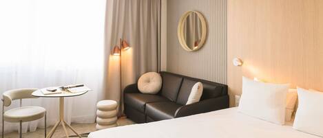Quarto de hotel com cama, sofá, mesa pequena e uma cadeira.