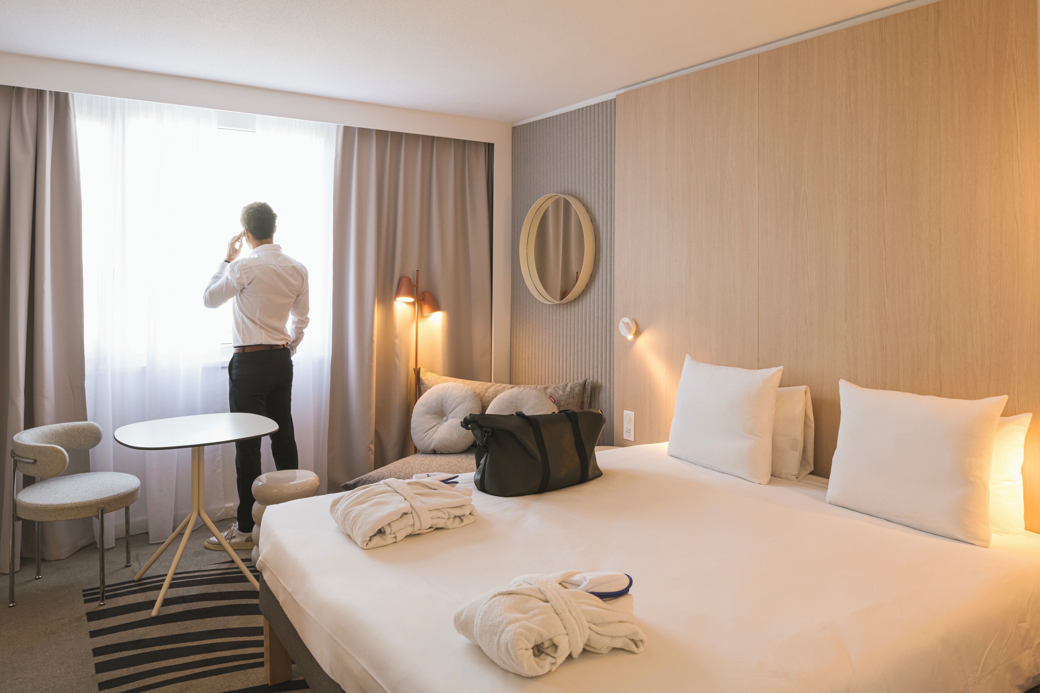 Quarto de hotel com cama, escrivaninha, cadeira, espelho e janela com cortinas.