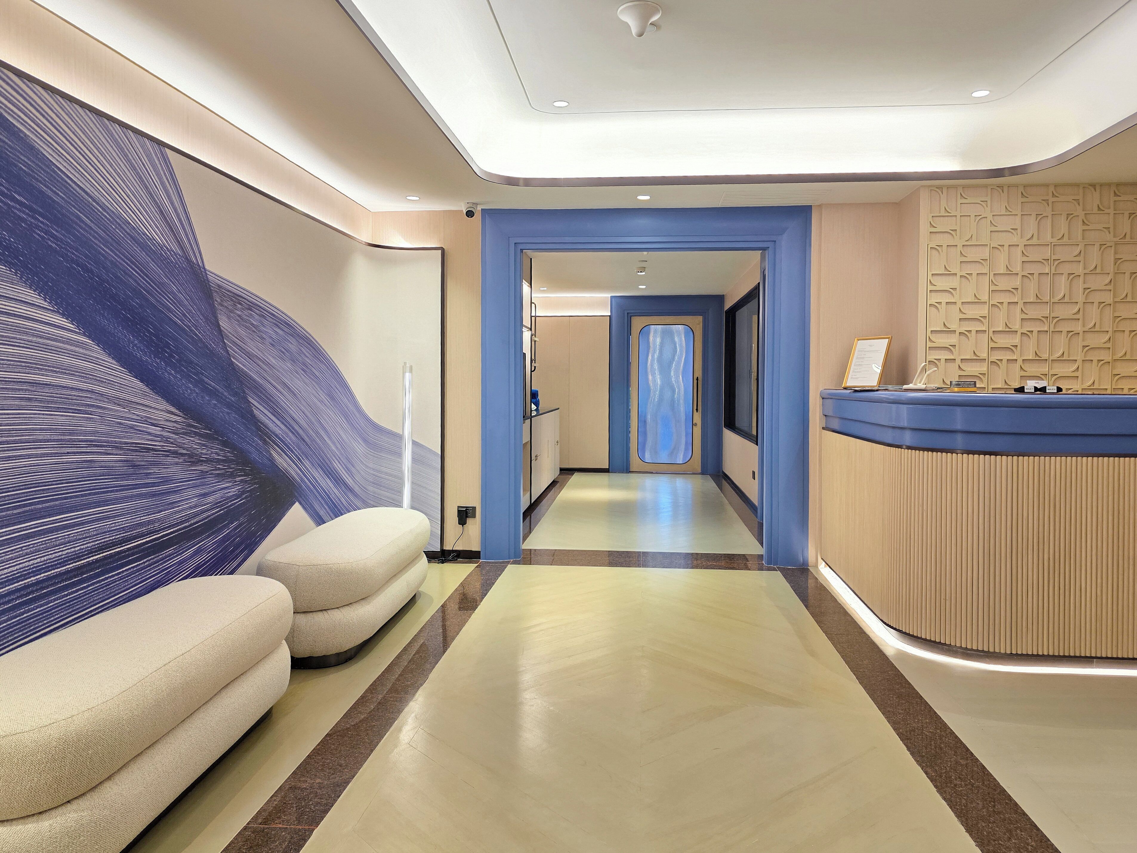 Um hall de hotel moderno, com uma mesa de recepção, área de estar com sofás e um painel de parede estampado.
