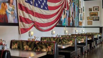 Interior de restaurante com decorações de bandeira americana, cabines com tema tropical e obras de arte emolduradas nas paredes.