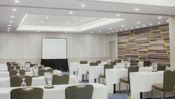 Uma sala de conferências com mesas, cadeiras, tela de projetor e quadro branco.
